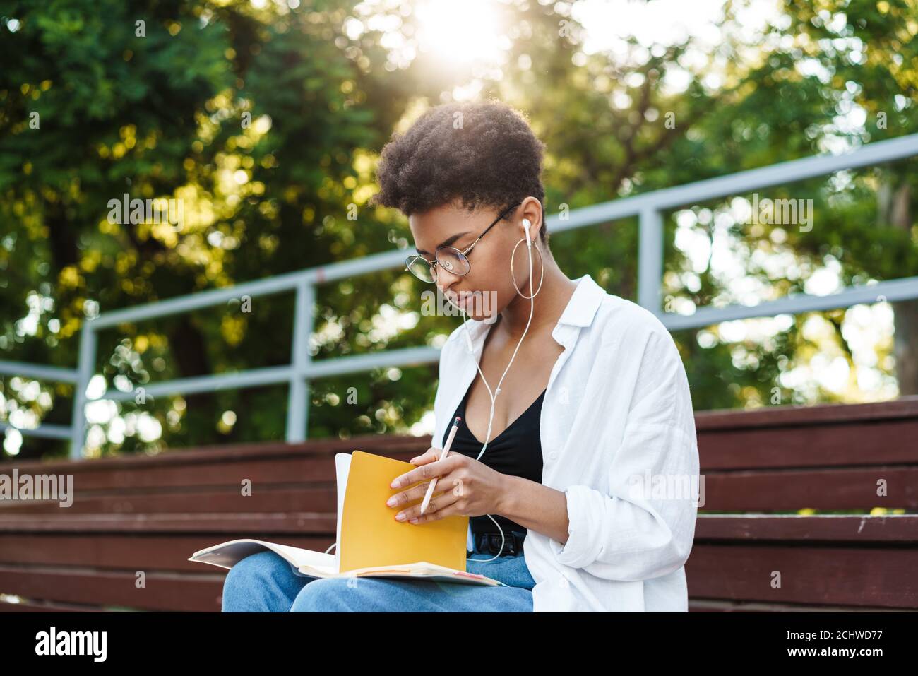 Photo of serious african woman sitting outdoors in park while writing ...