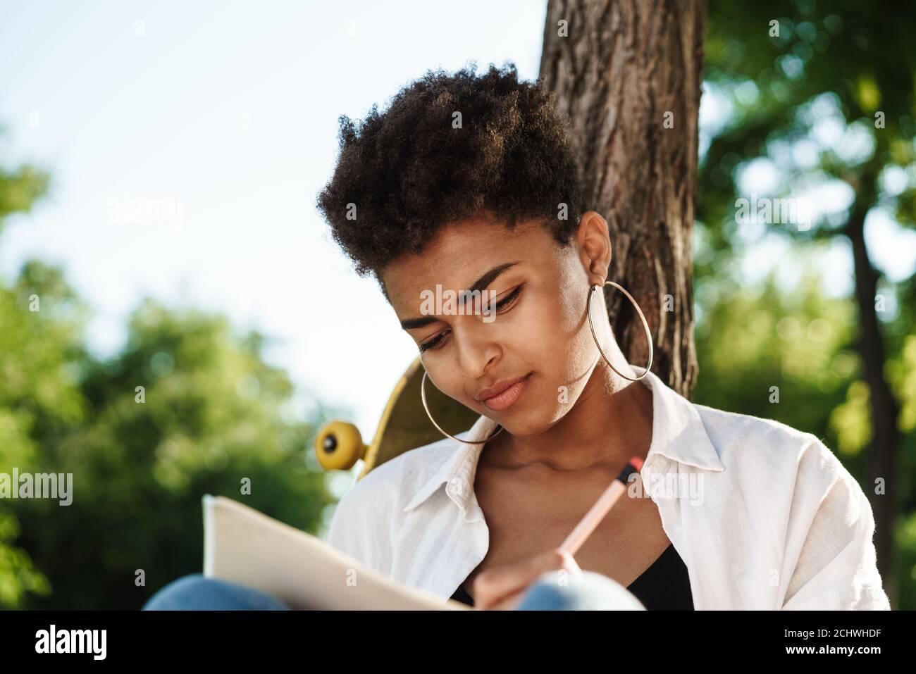 Attractive smiling young african womam writing in a diary in the park ...