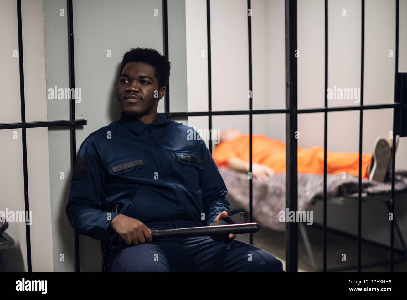 A strong black prison guard guards the cells with prisoners in the ...