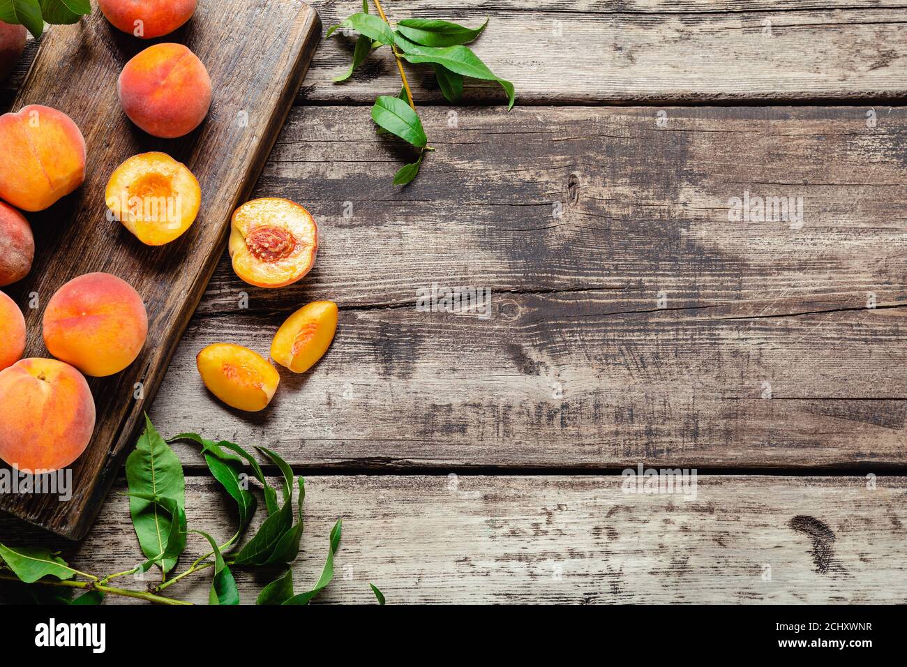 Peaches with leaves on dark wooden board with peach in halves ...