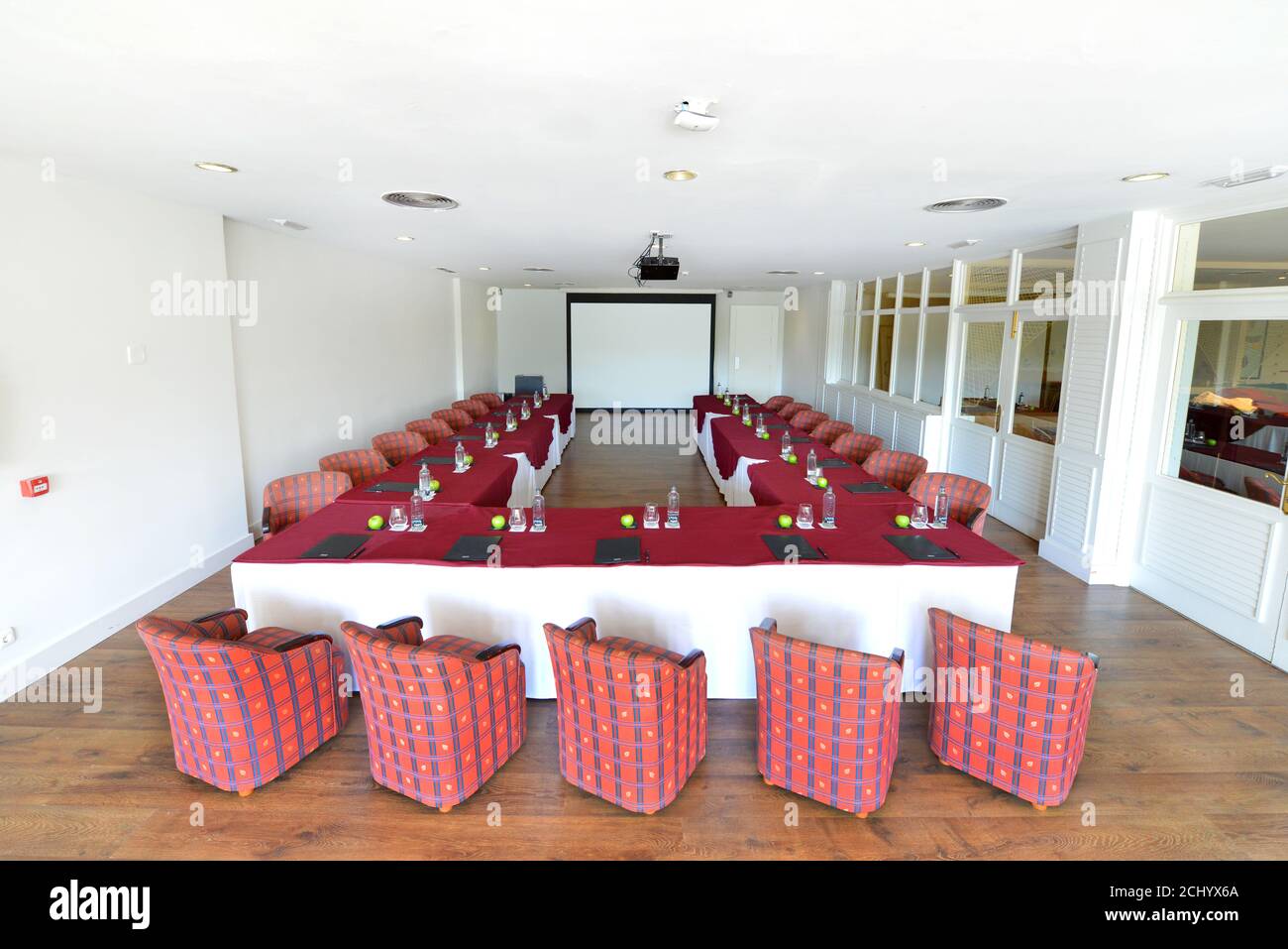 Inside of a conference hall with set-up chairs and tables and a screen ...