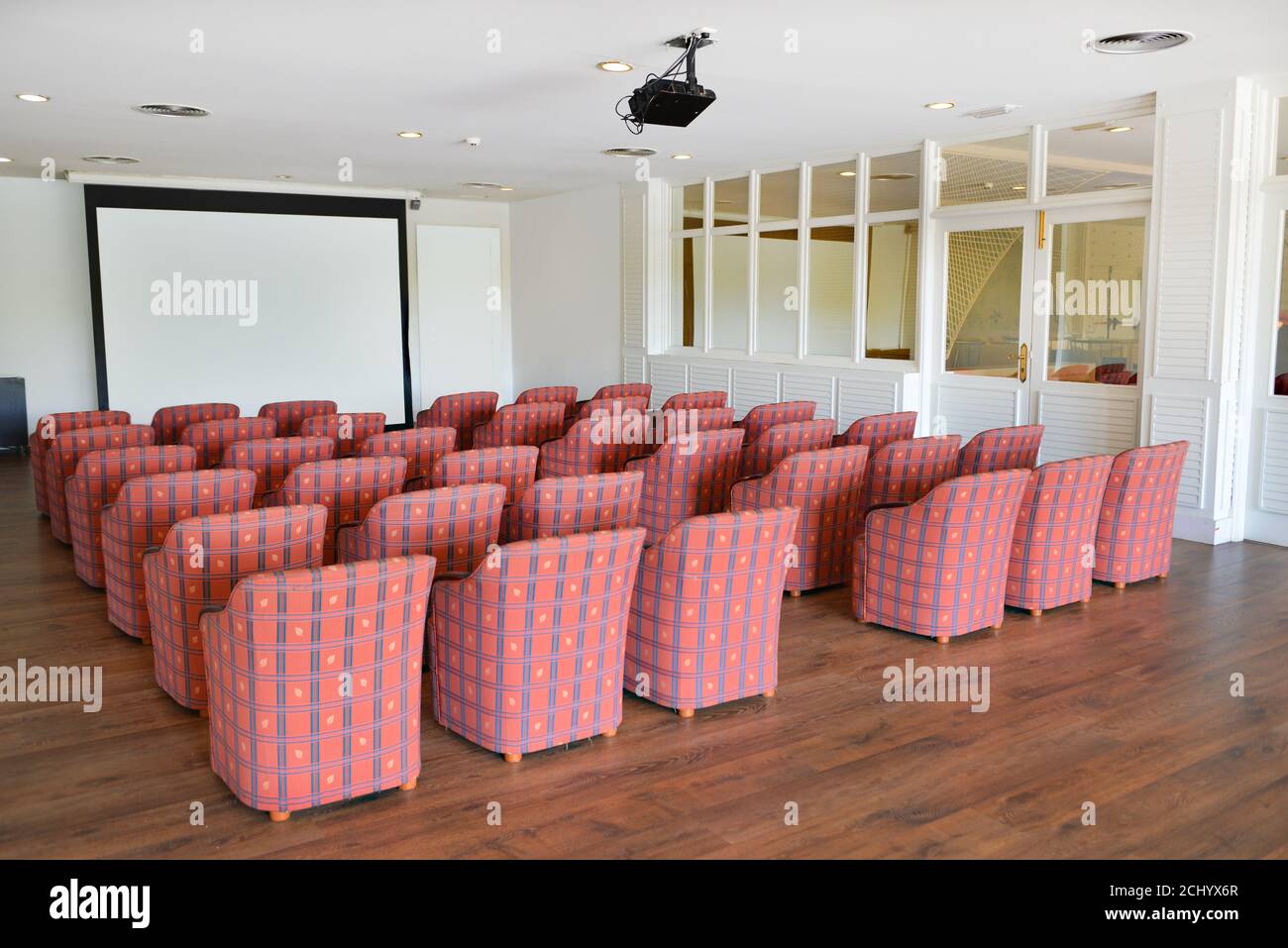 Inside of a conference hall with set-up chairs and a screen on the wall ...