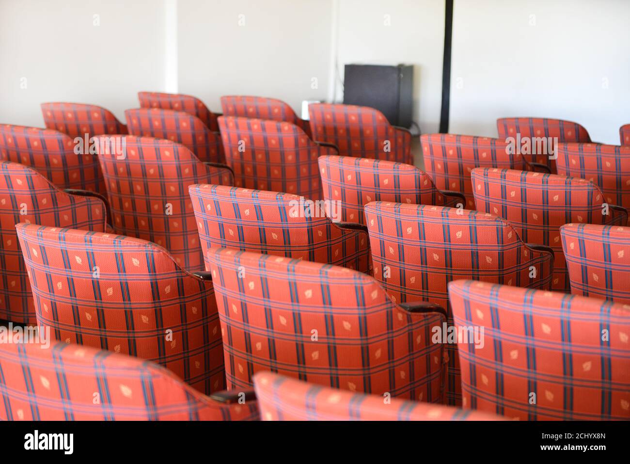 Inside of a conference hall with set-up chairs and a screen on the wall ...