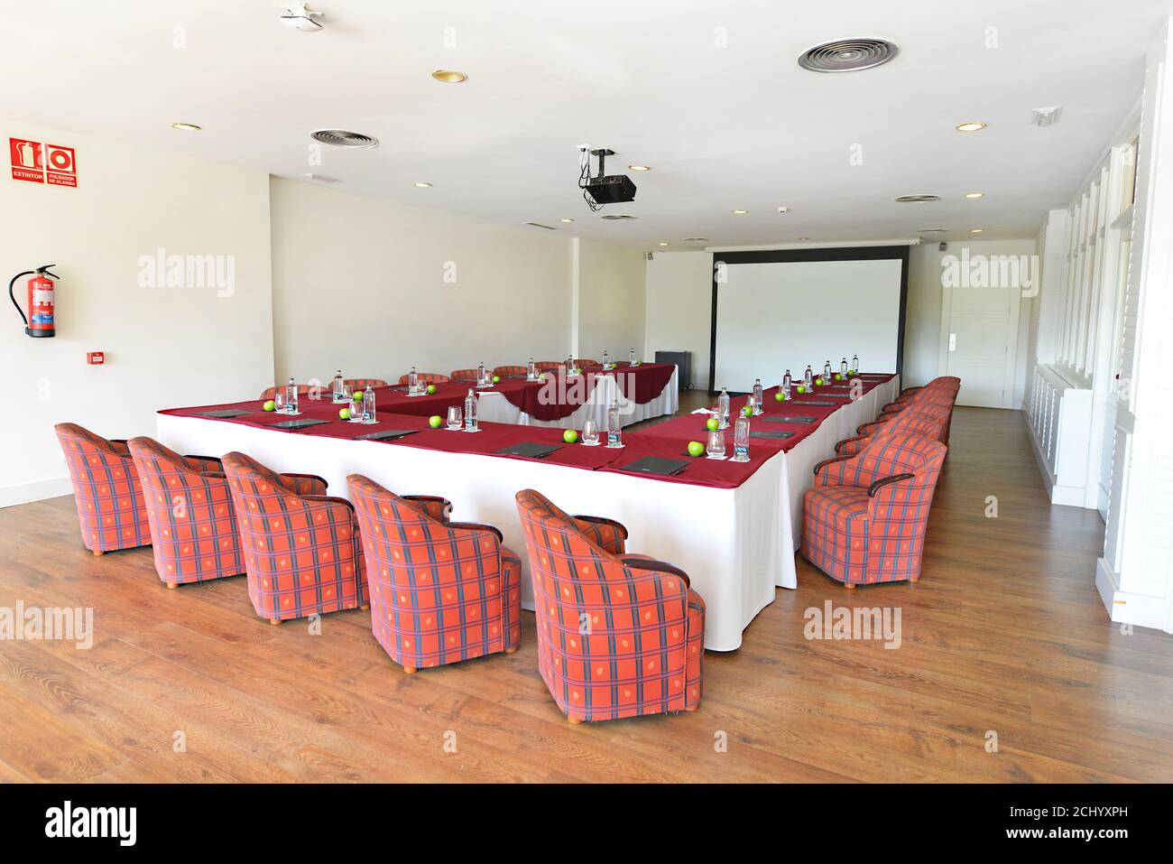 Inside of a conference hall with set-up chairs and tables and a screen ...
