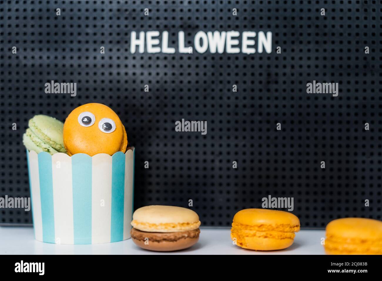 Tasty Halloween macaroons with funny face and eyes in paper cup on the ...