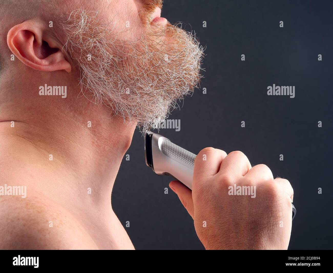 Bearded man with trimmer to adjust beard in hand Stock Photo - Alamy