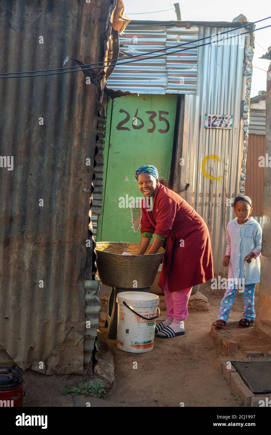 African woman and young child washing clothes in Diepsloot township ...