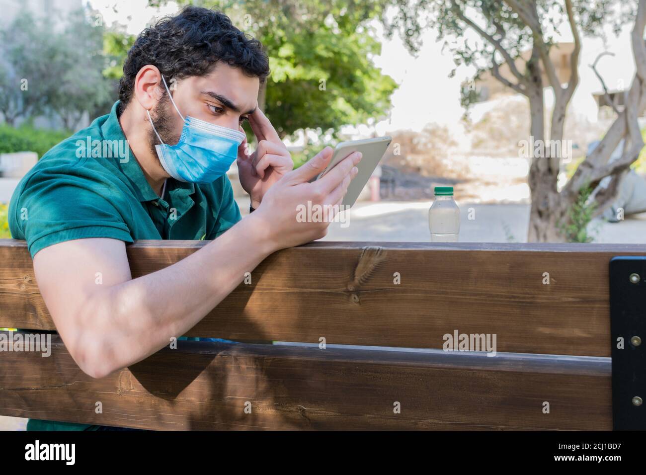 Bored Caucasian male sitting in a park while checking his mobile phone ...