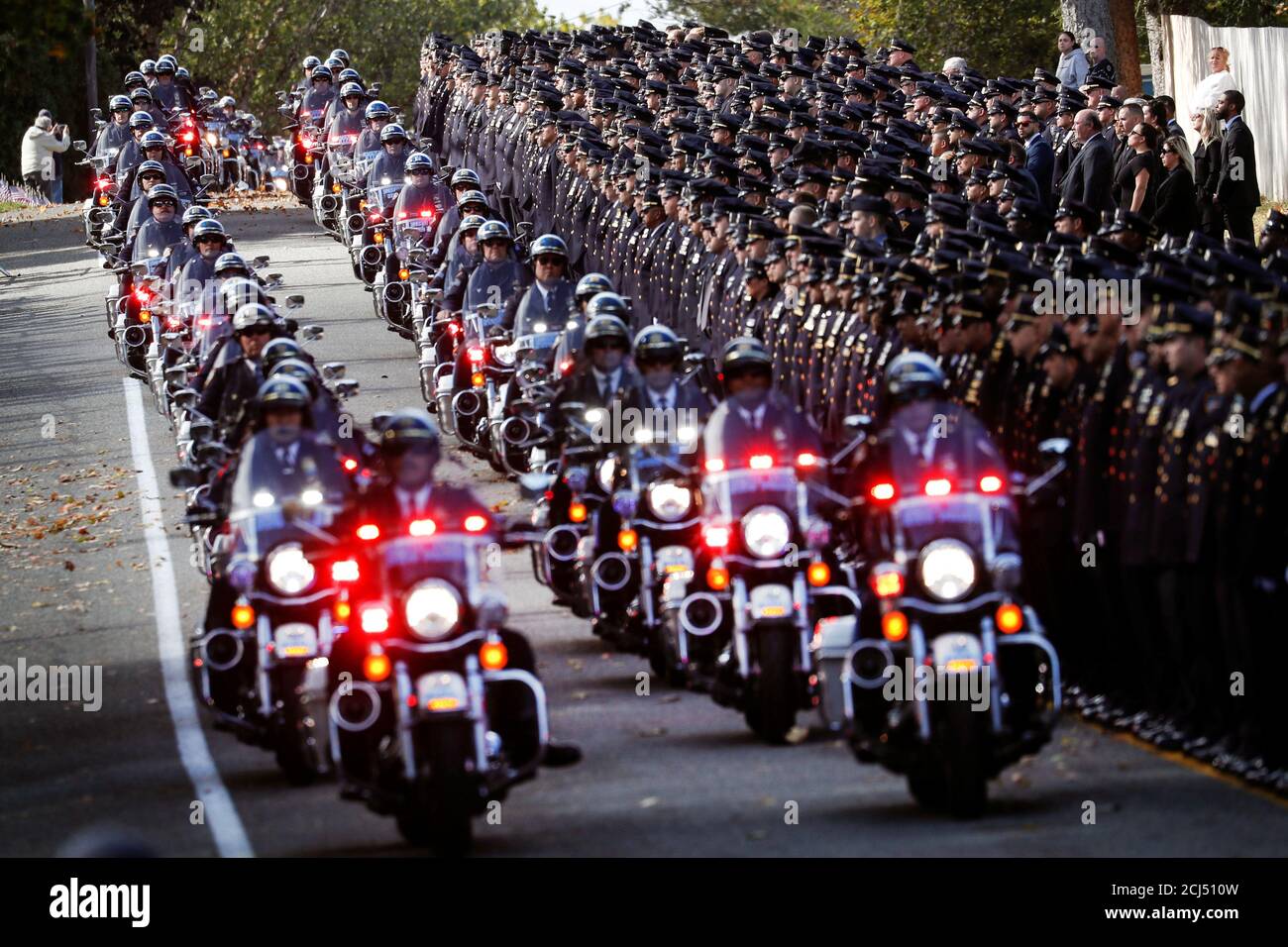 A procession of police motorcycles passes officers lining the street at ...