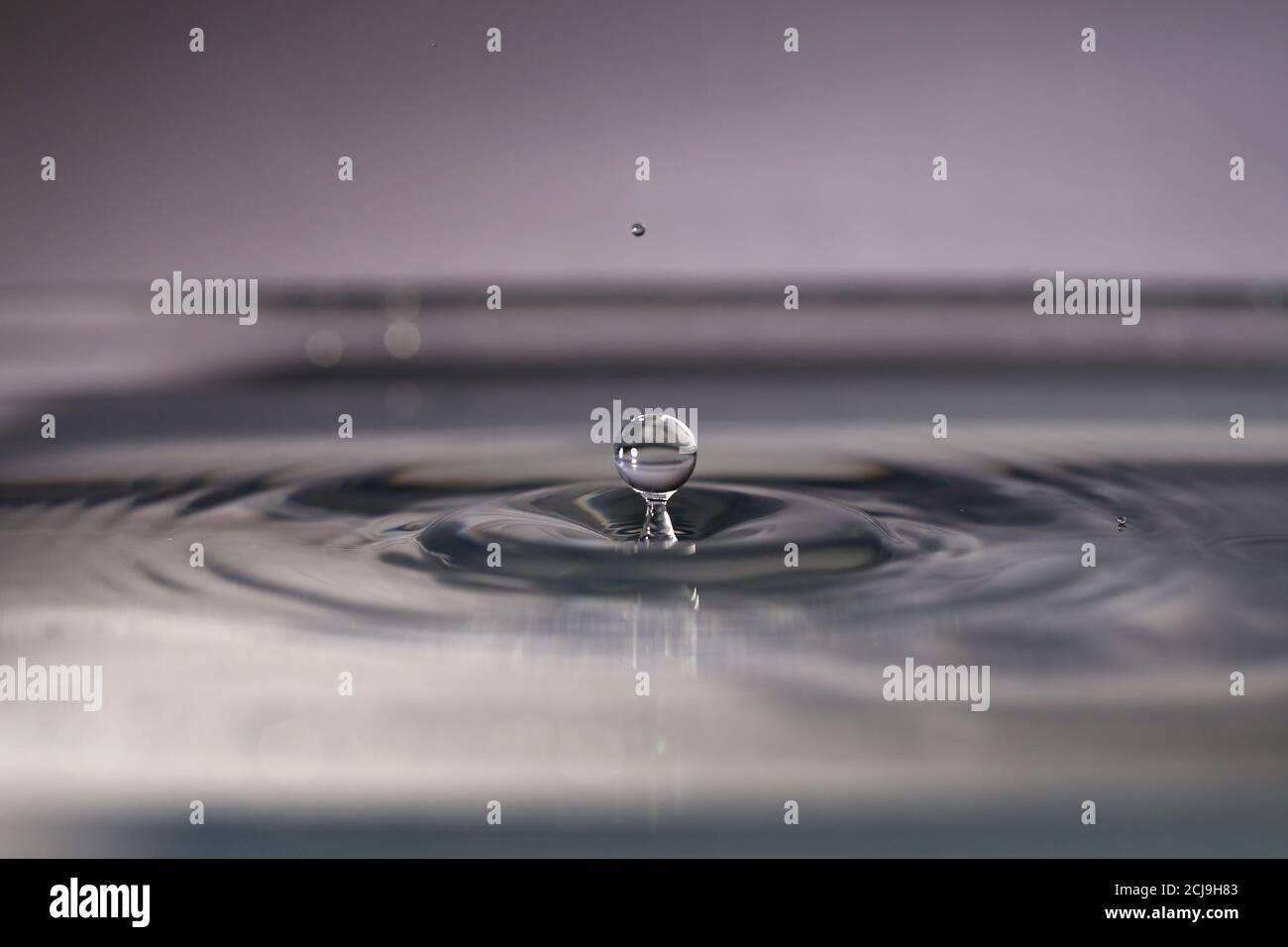 Small water drop fall on water surface creating a splash and ripples ...