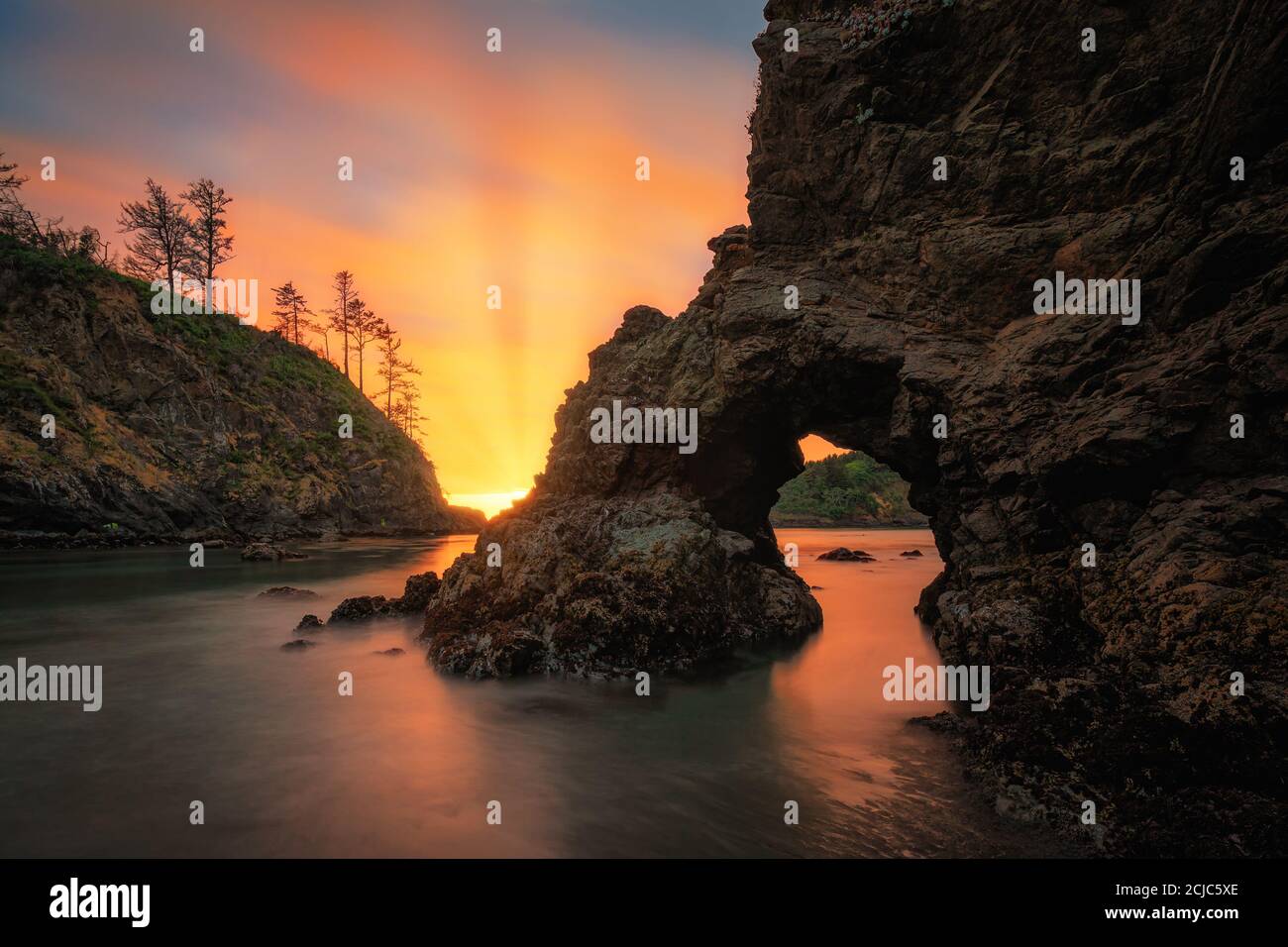 Sunset over a natural arch at the beach Stock Photo - Alamy