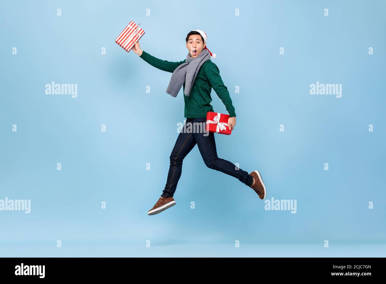 Asian man in Christmas sweater jumping and holding gift boxes isolated ...