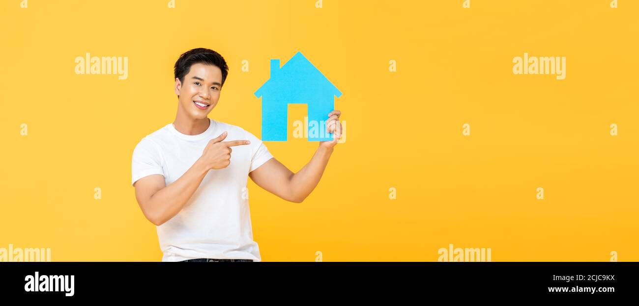 Handsome Asian man holding and pointing to house cutout isolated on ...