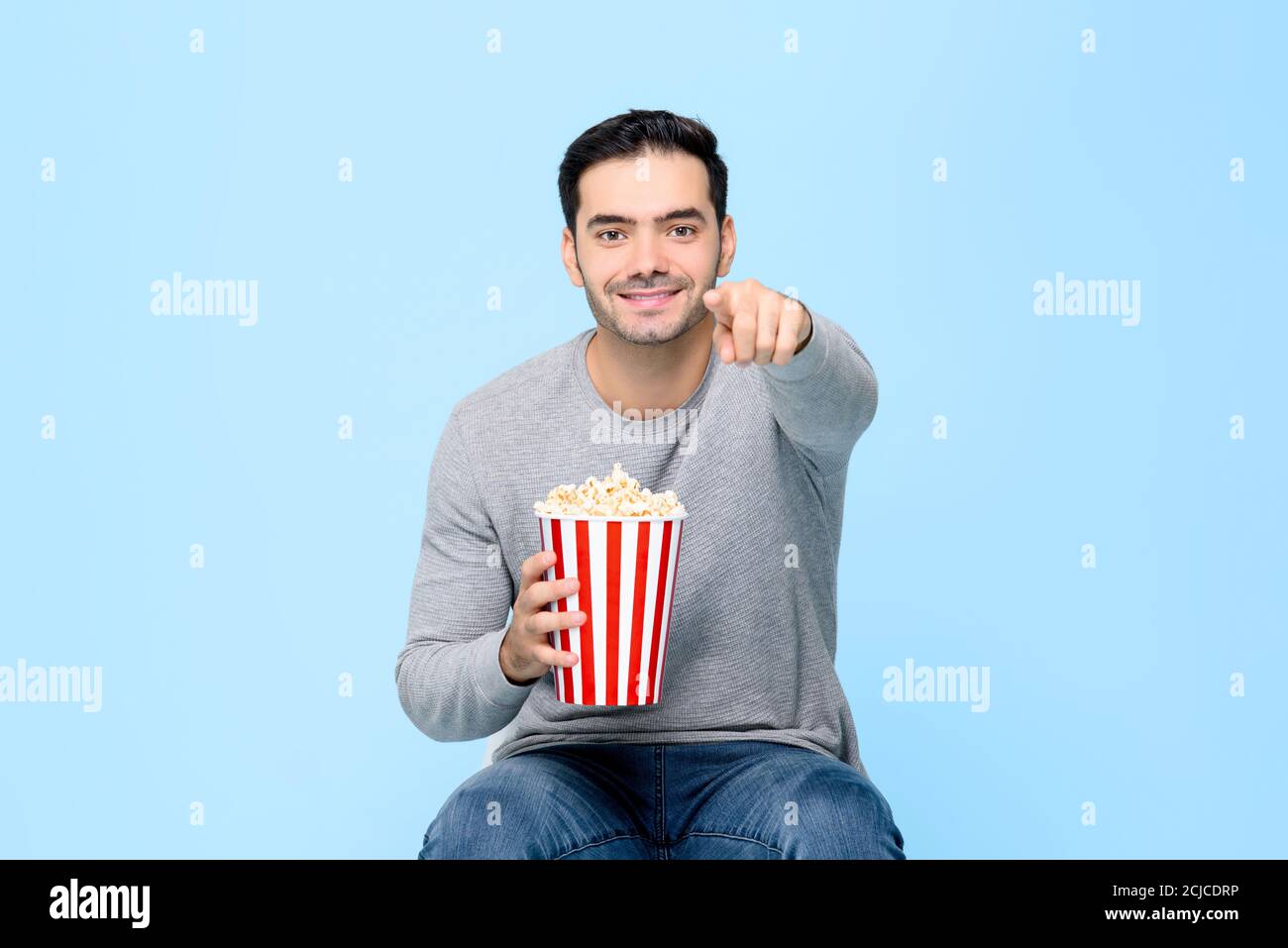 Amused young Caucasian man holding popcorn and pointing while watching ...