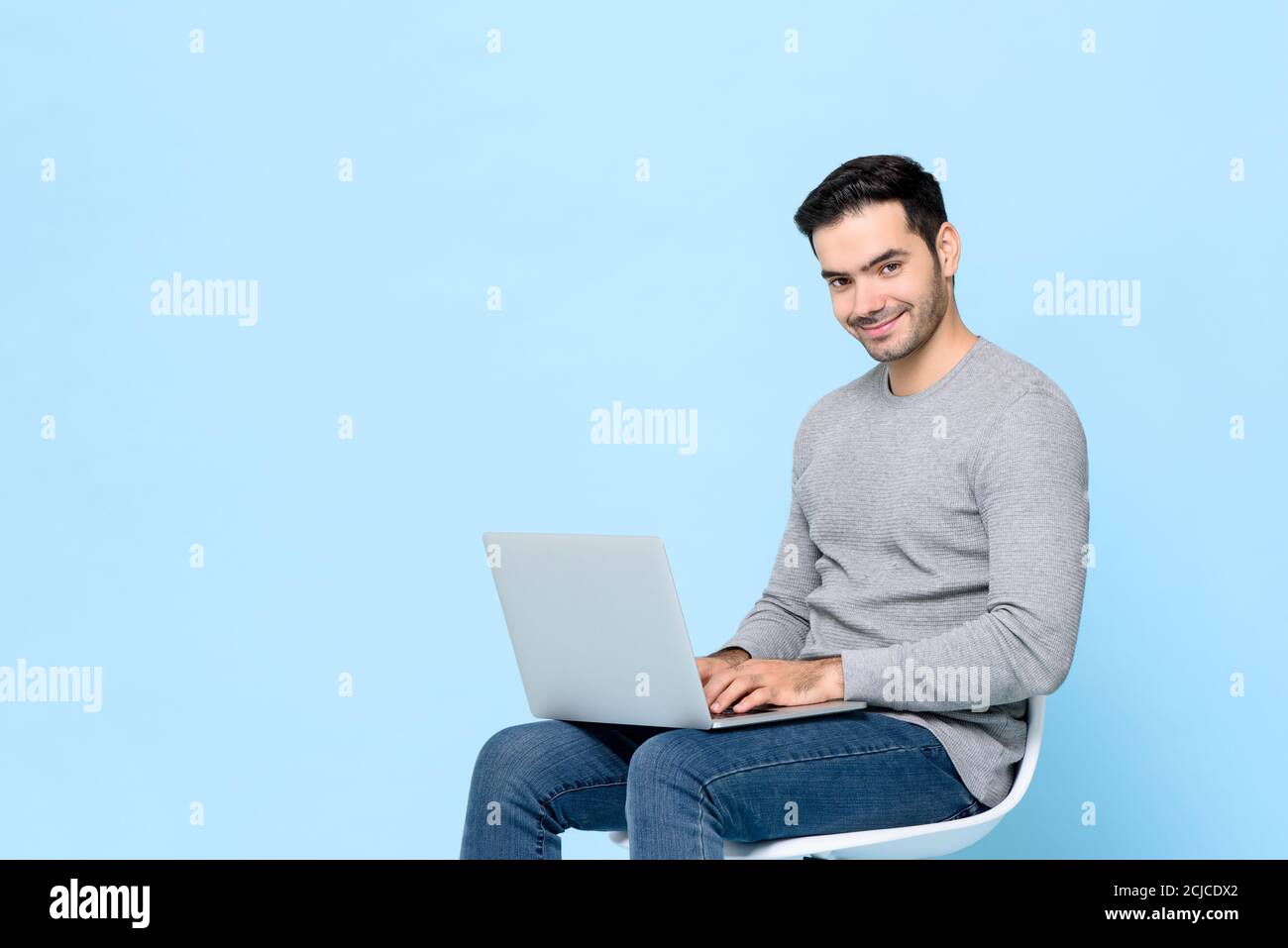 Smiling handsome man sitting typing on laptop computer in isolated ...