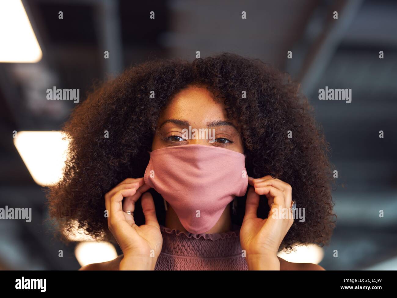 Portrait Of Businesswoman Putting On Face Mask In Modern Open Plan ...