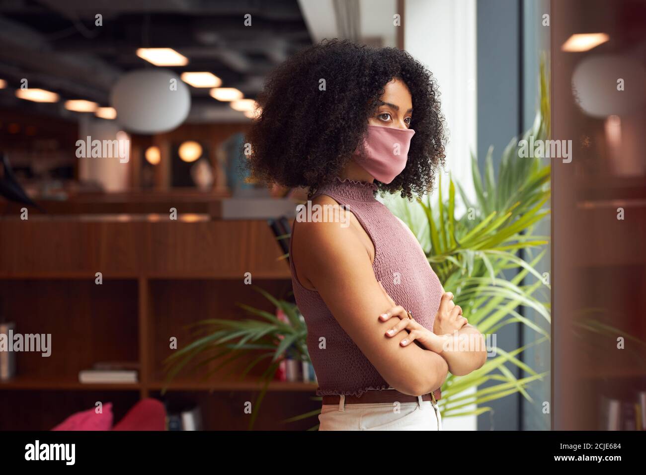 Businesswoman By Window Wearing Face Mask In Modern Open Plan Office ...