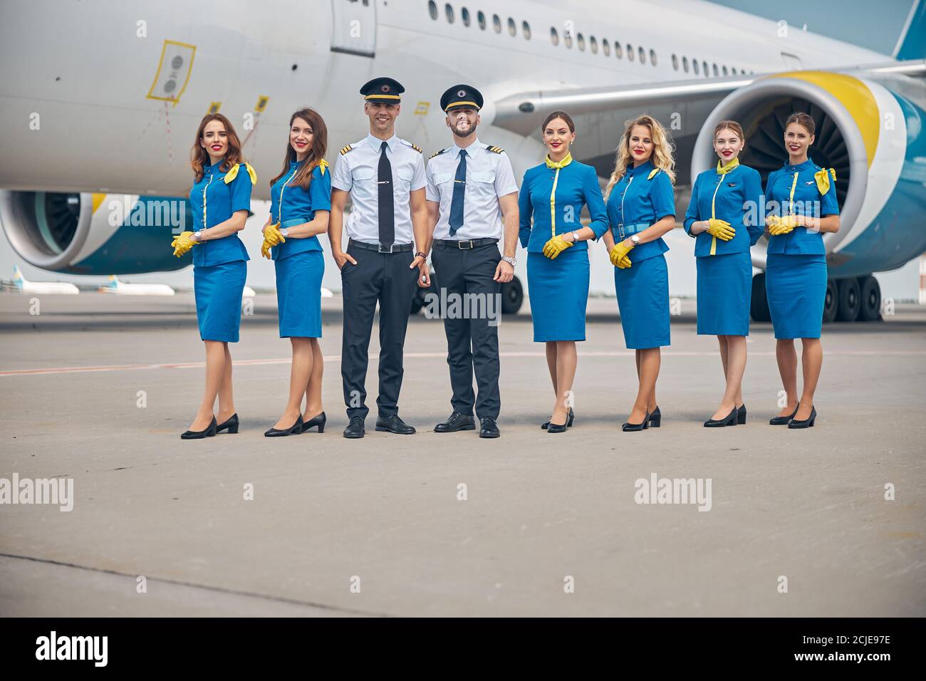 Handsome pilots and beautiful stewardesses standing outdoors in ...