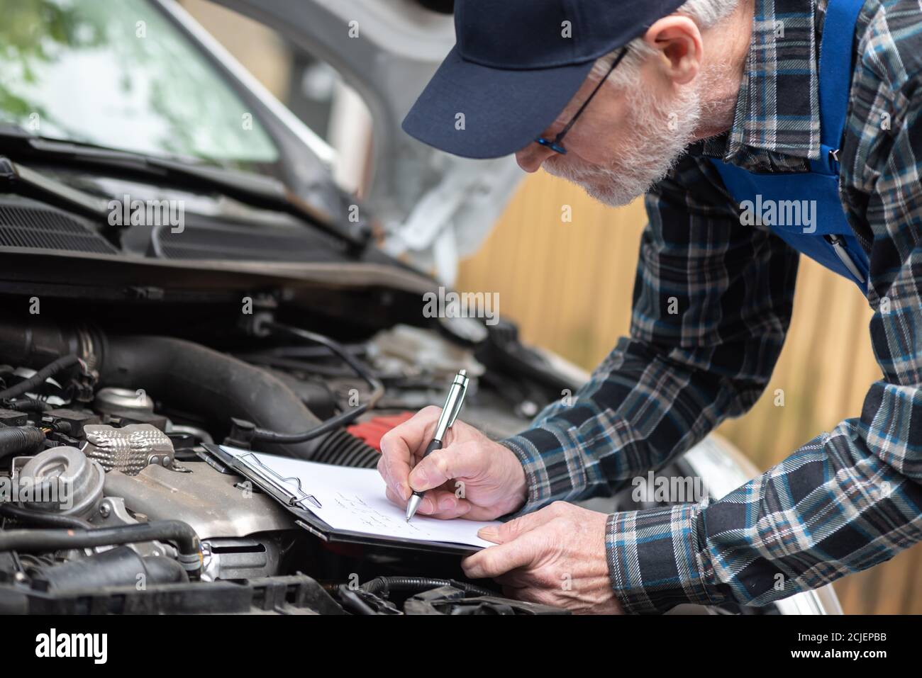 Car mechanic checking a car engine and writing on clipboard Stock Photo ...