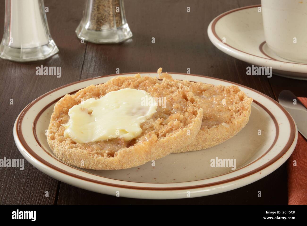 A toasted and buttered whole grain English muffin with a cup of coffee ...