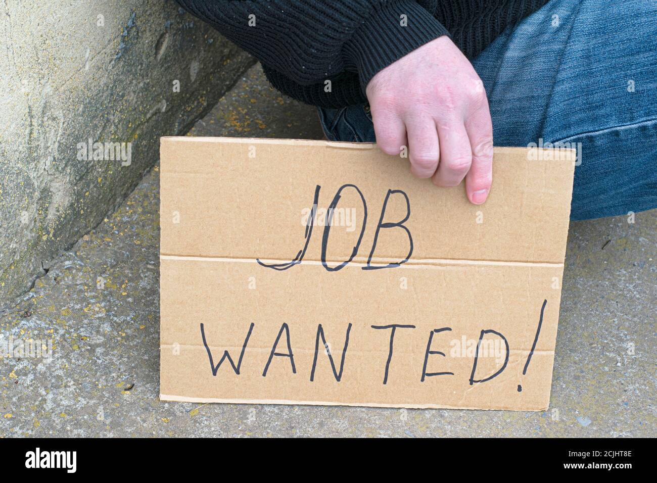 unemployed man sitting on the ground holding a cardboard sign saying ...