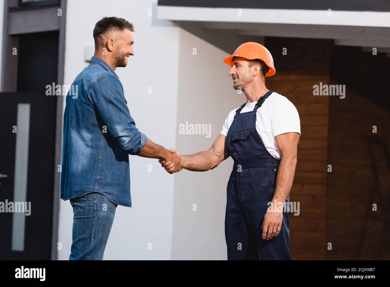 Man shaking hands with builder in uniform near building Stock Photo - Alamy