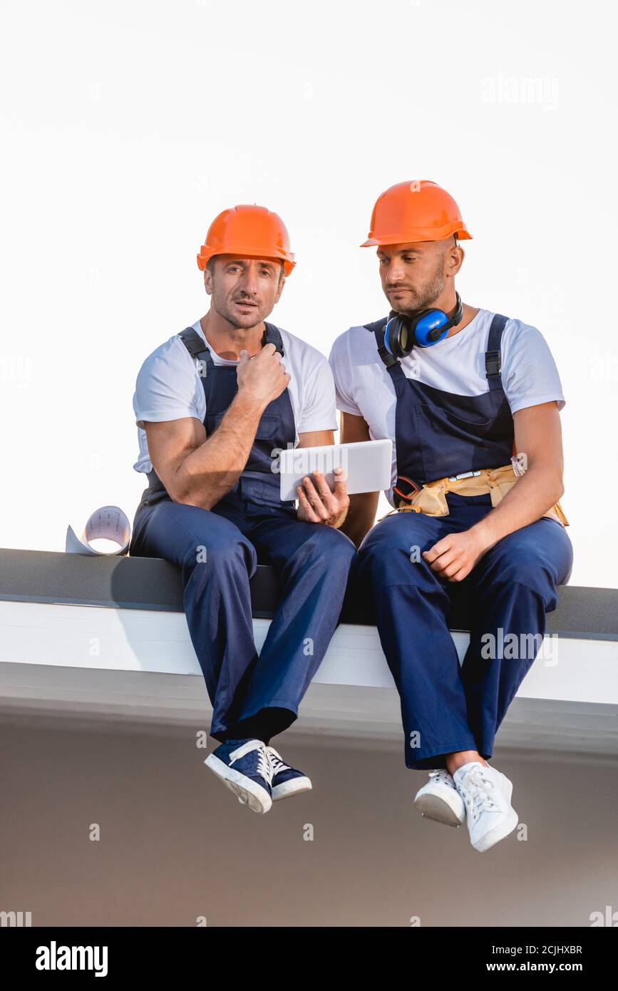 Builders using digital tablet while sitting on roof of building ...