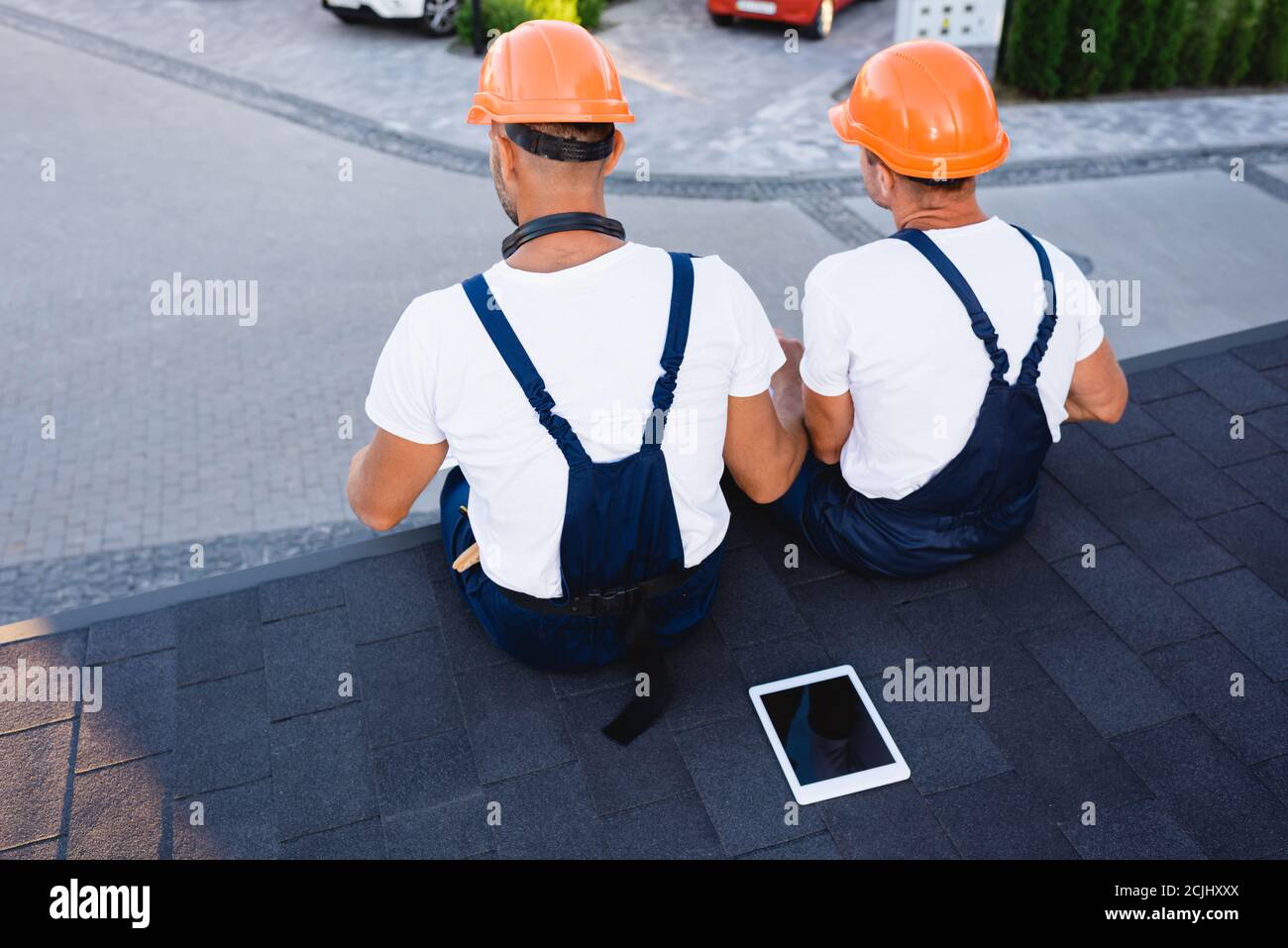 Back view of builders sitting near digital tablet on roof of building ...
