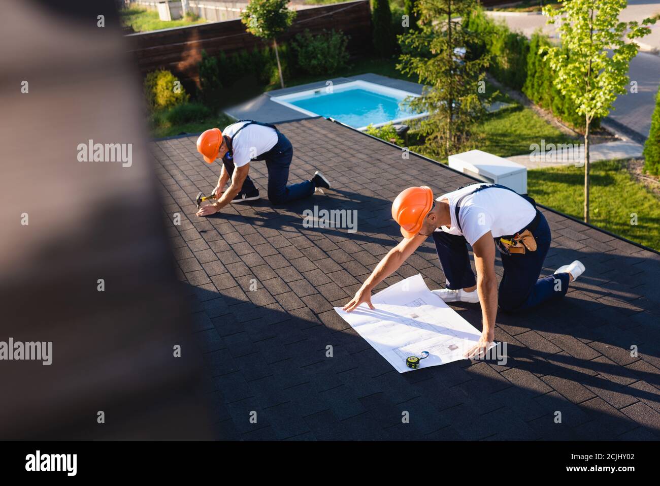 Selective focus of builders with blueprint and tools working on roof of ...