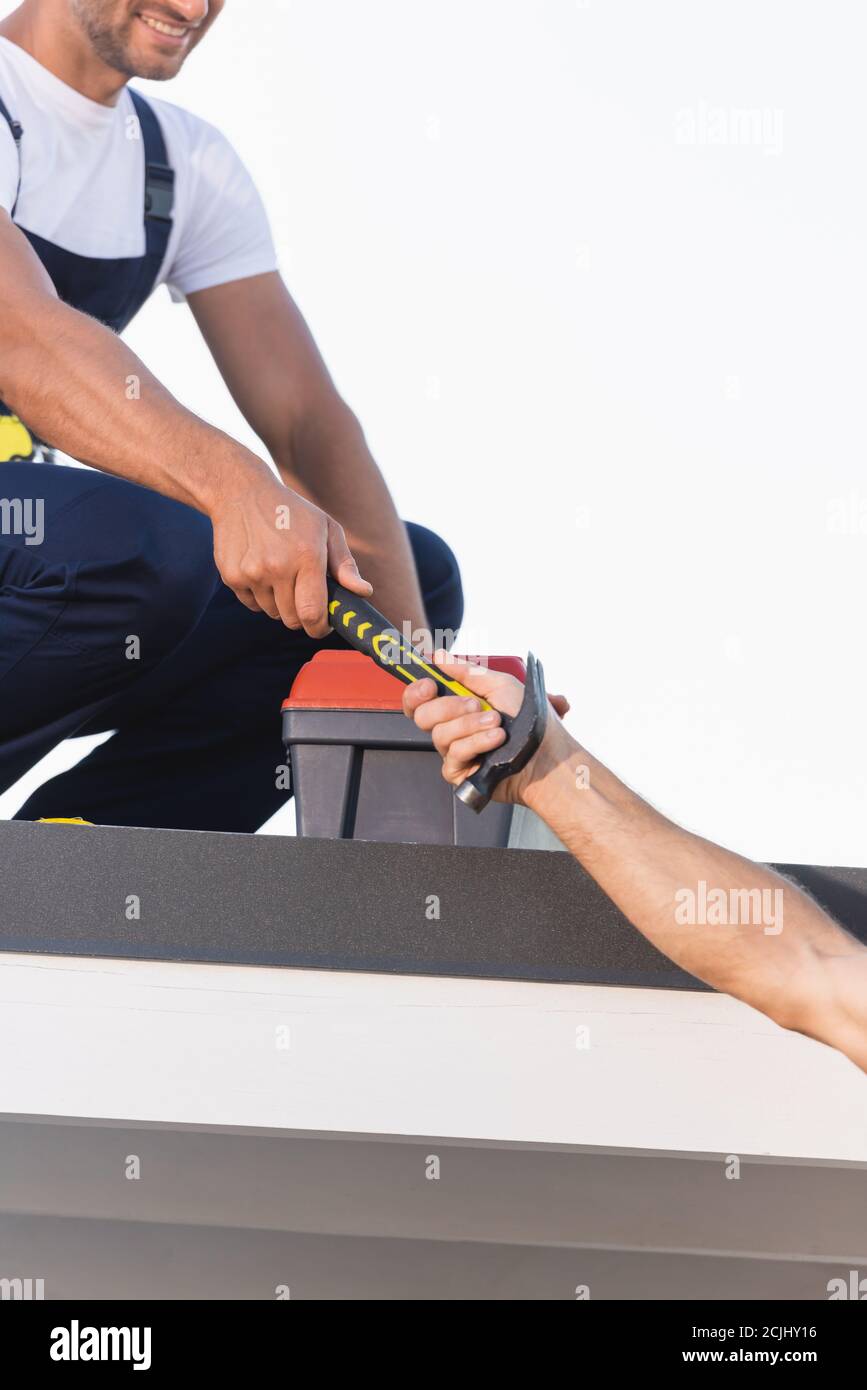 Cropped view of builder giving hammer to colleague near toolbox on roof ...