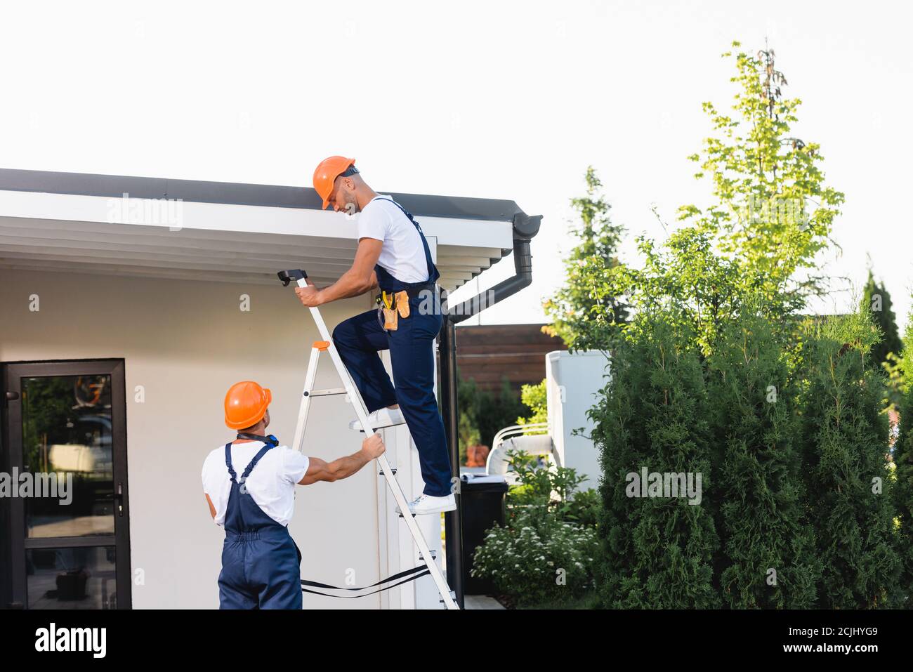 Builders using ladder near facade and roof of building on urban street ...