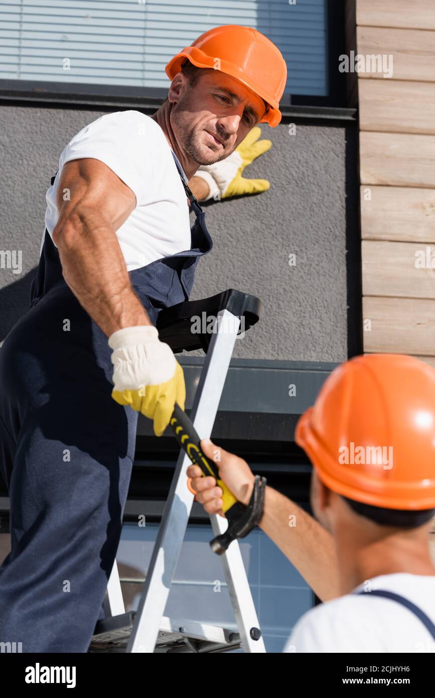 Selective focus of builder giving hammer to colleague on ladder near ...
