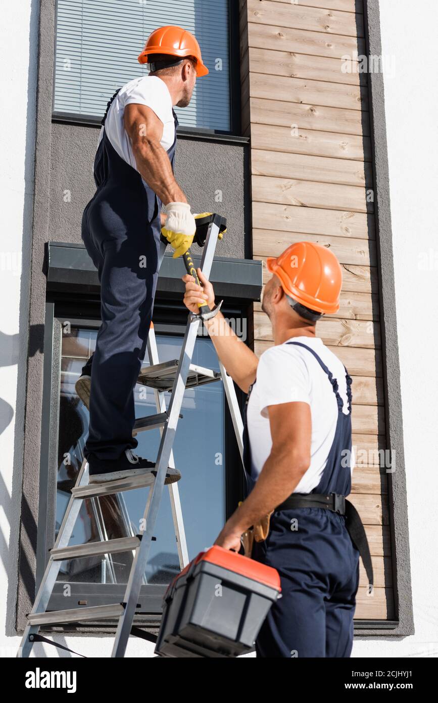 Selective focus of workman with toolbox giving hammer to colleague on ...