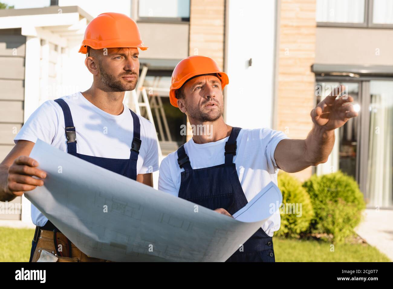 Builder pointing with hand near colleague with blueprint outdoors Stock ...