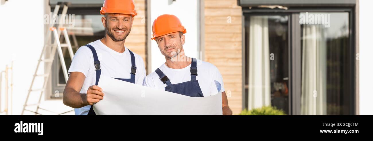 Horizontal crop of builders in hardhats holding blueprint outdoors ...
