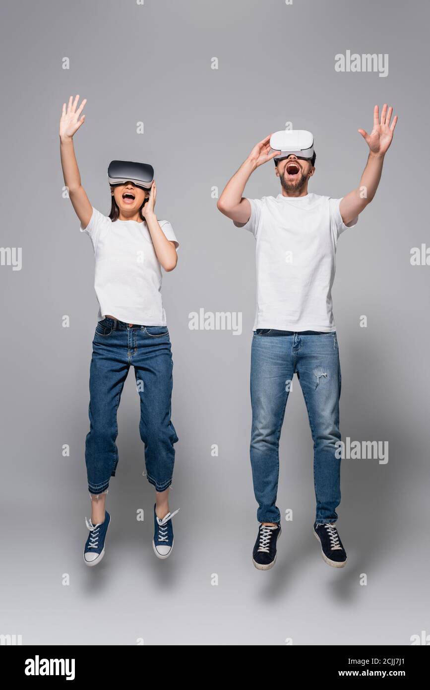 excited couple in vr headsets, jeans and white t-shirts waving hands ...