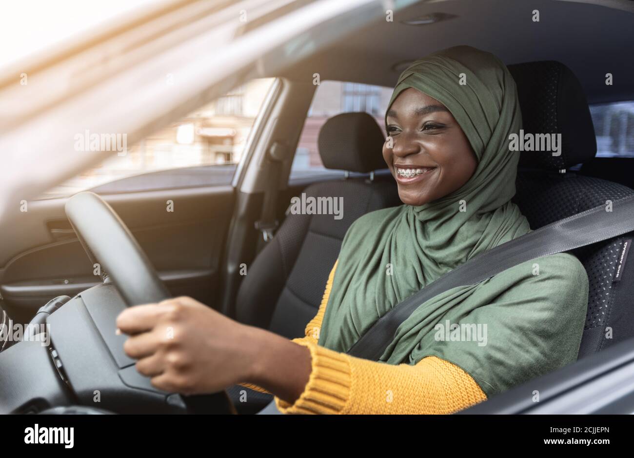 Happy Black Muslim Woman In Hijab Driving Car With Fasten Seat Belt ...