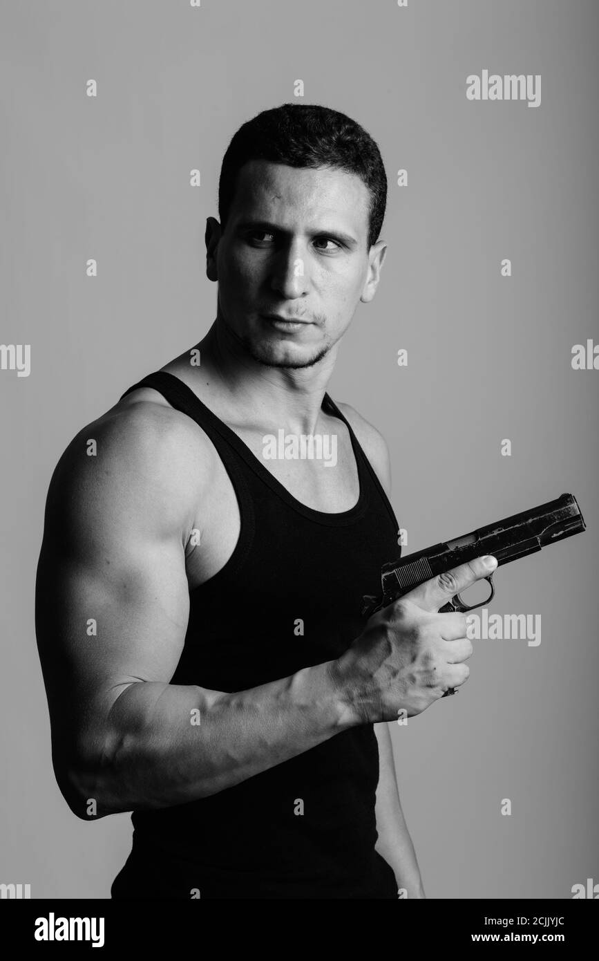 Studio shot of young muscular Persian man thinking while holding gun ...