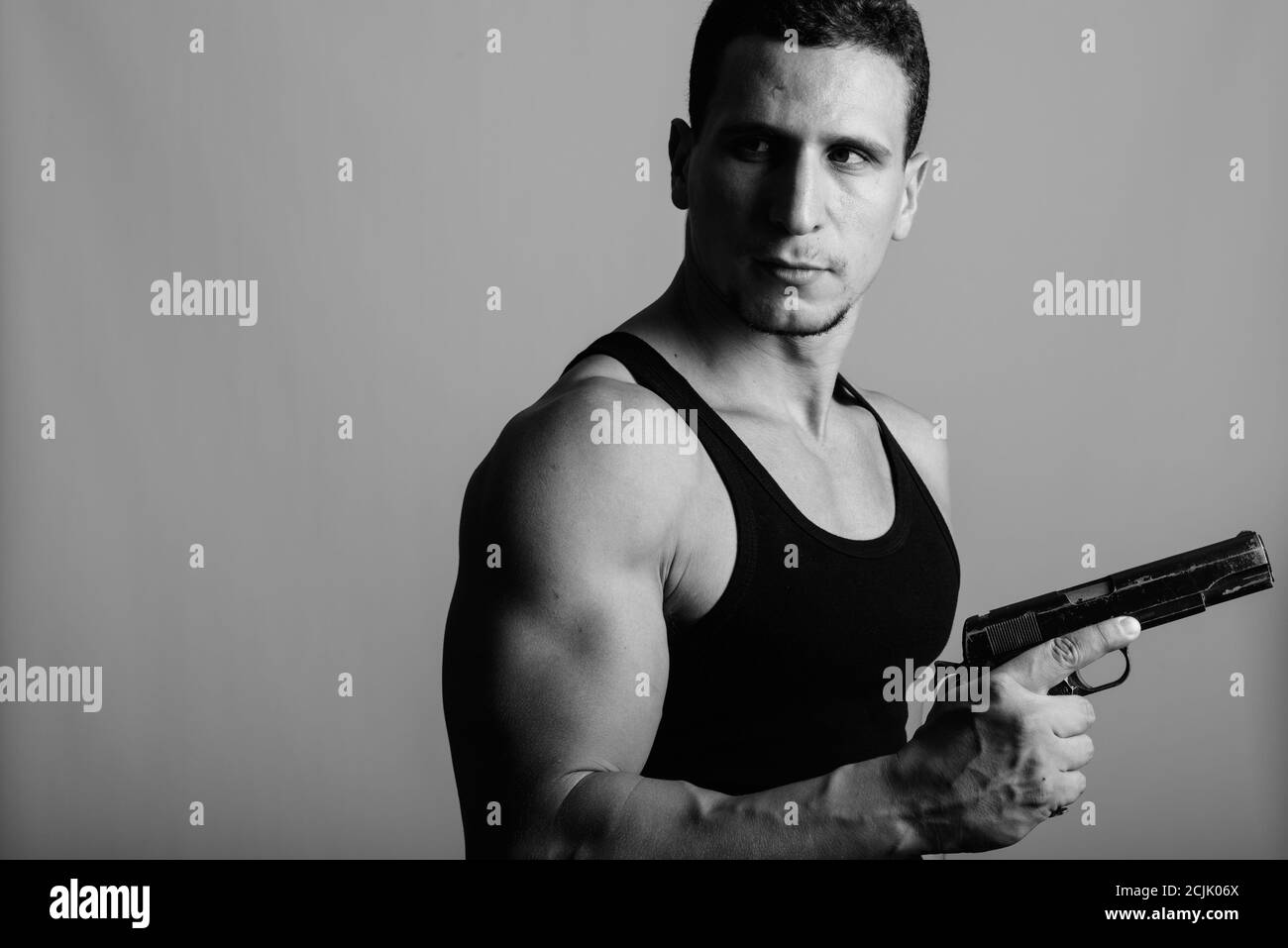 Studio shot of young muscular Persian man holding gun and thinking ...