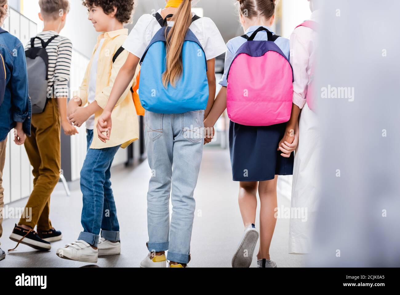 back view of multiethnic classmates holding hands while walking along ...