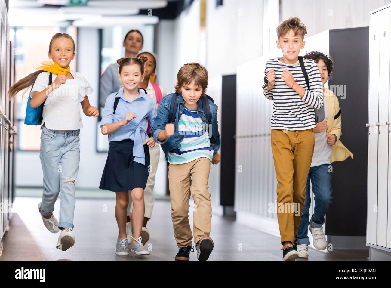 excited multicultural pupils running along school corridor with teacher ...
