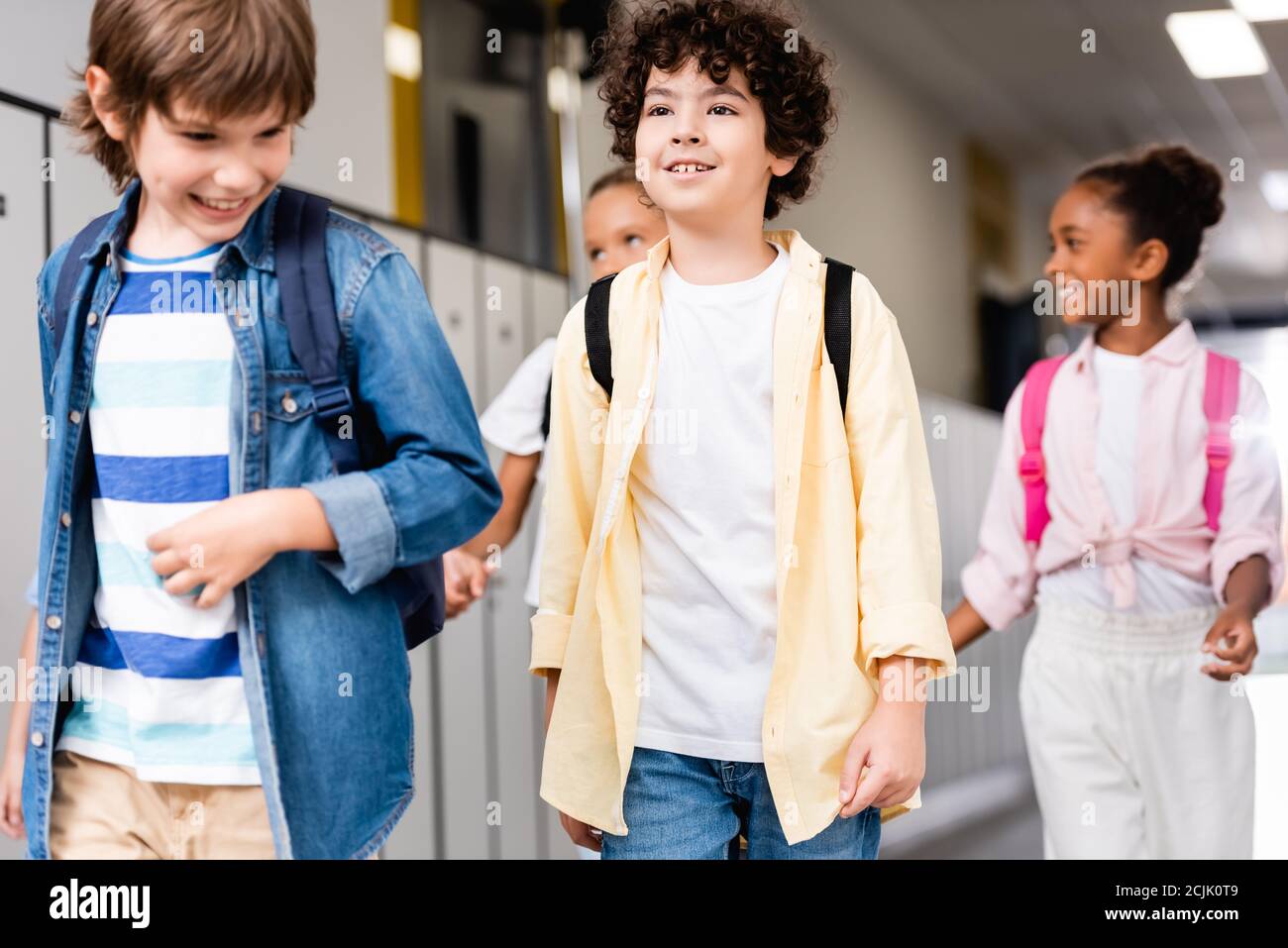 excited multicultural schoolchildren walking along school corridor ...