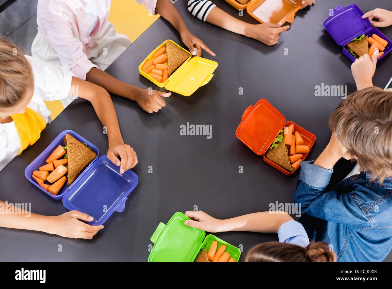 overhead view of multicultural classmates sitting in school eatery near ...