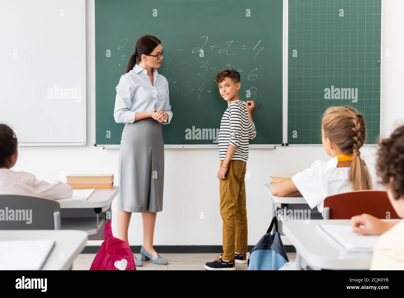 schoolboy looking at multicultural classmates while solving equations ...