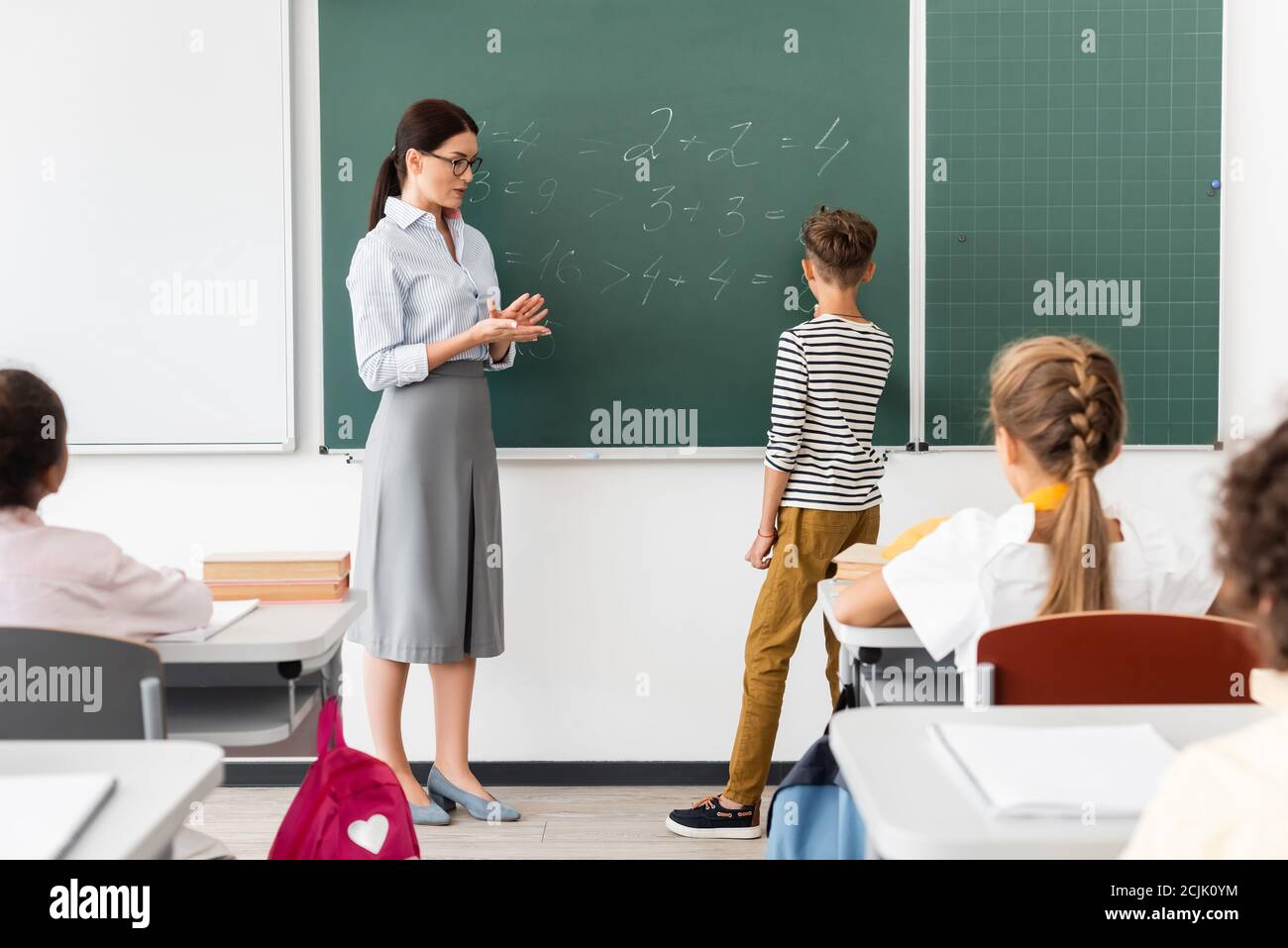 back view of schoolboy solving equations on chalkboard during math ...