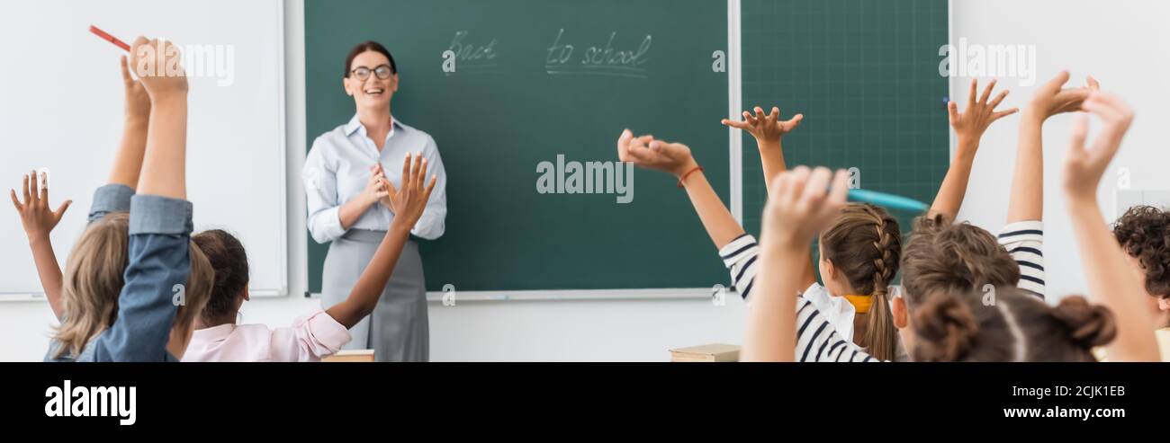 back view of multicultural pupils with hands in air, and teacher ...