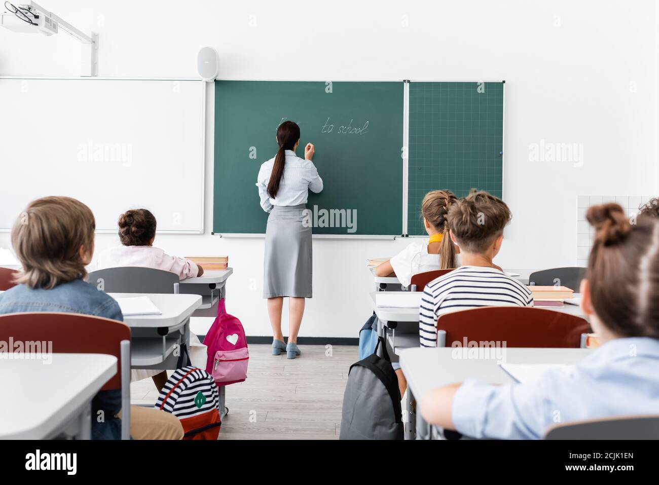 back view of teacher in formal wear writing on chalkboard near ...
