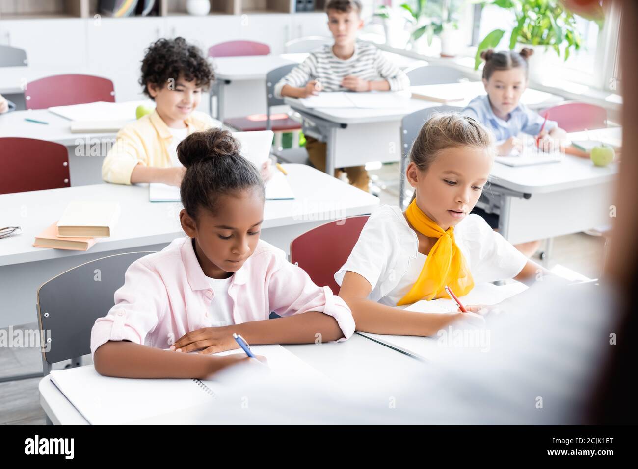 selective focus of multicultural pupils writing in notebooks during ...