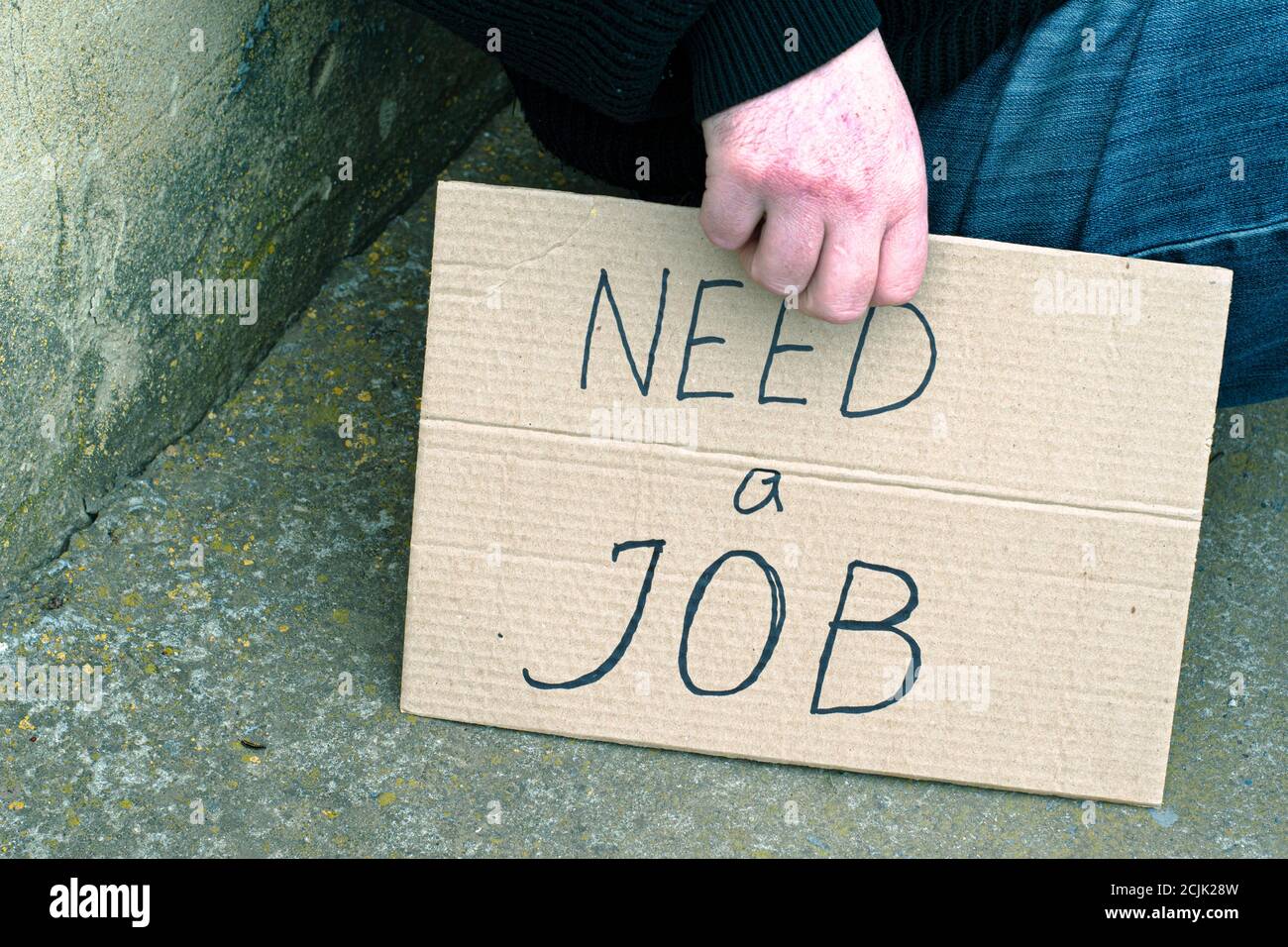 unemployed man sitting on the ground holding a cardboard sign saying ...
