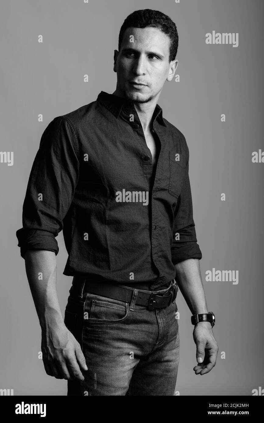 Studio shot of young muscular Persian man standing while thinking and ...